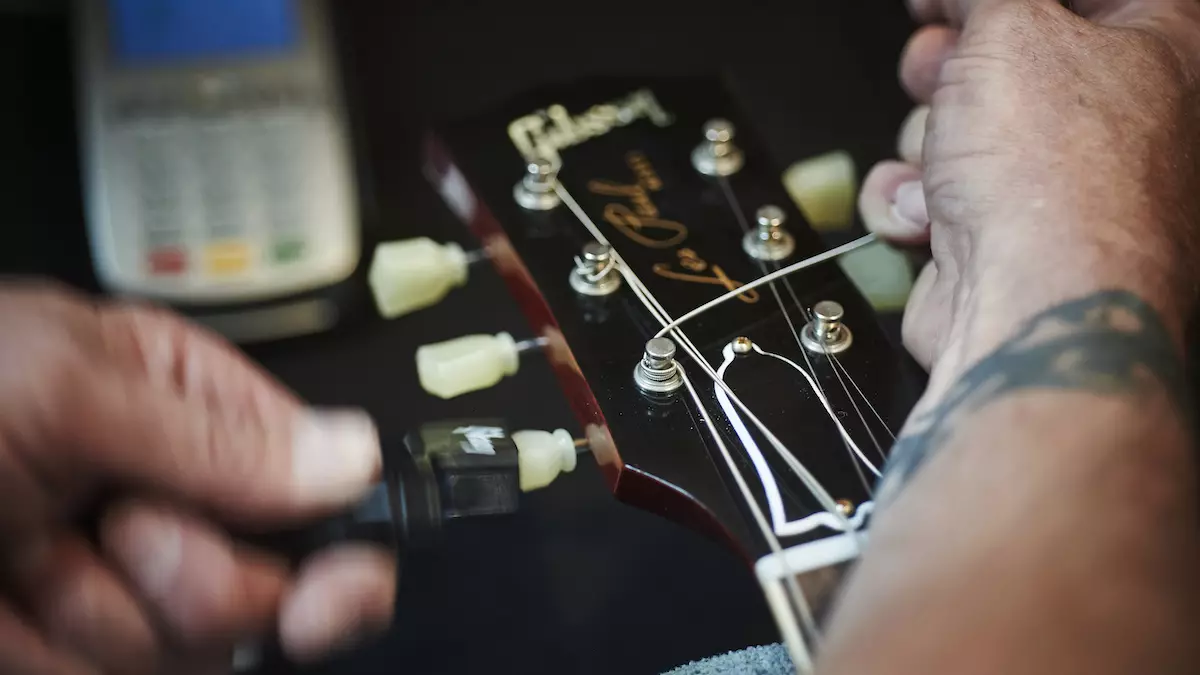 El hombre usa un devanador de cuerdas para colocar una cuerda nueva en su guitarra eléctrica